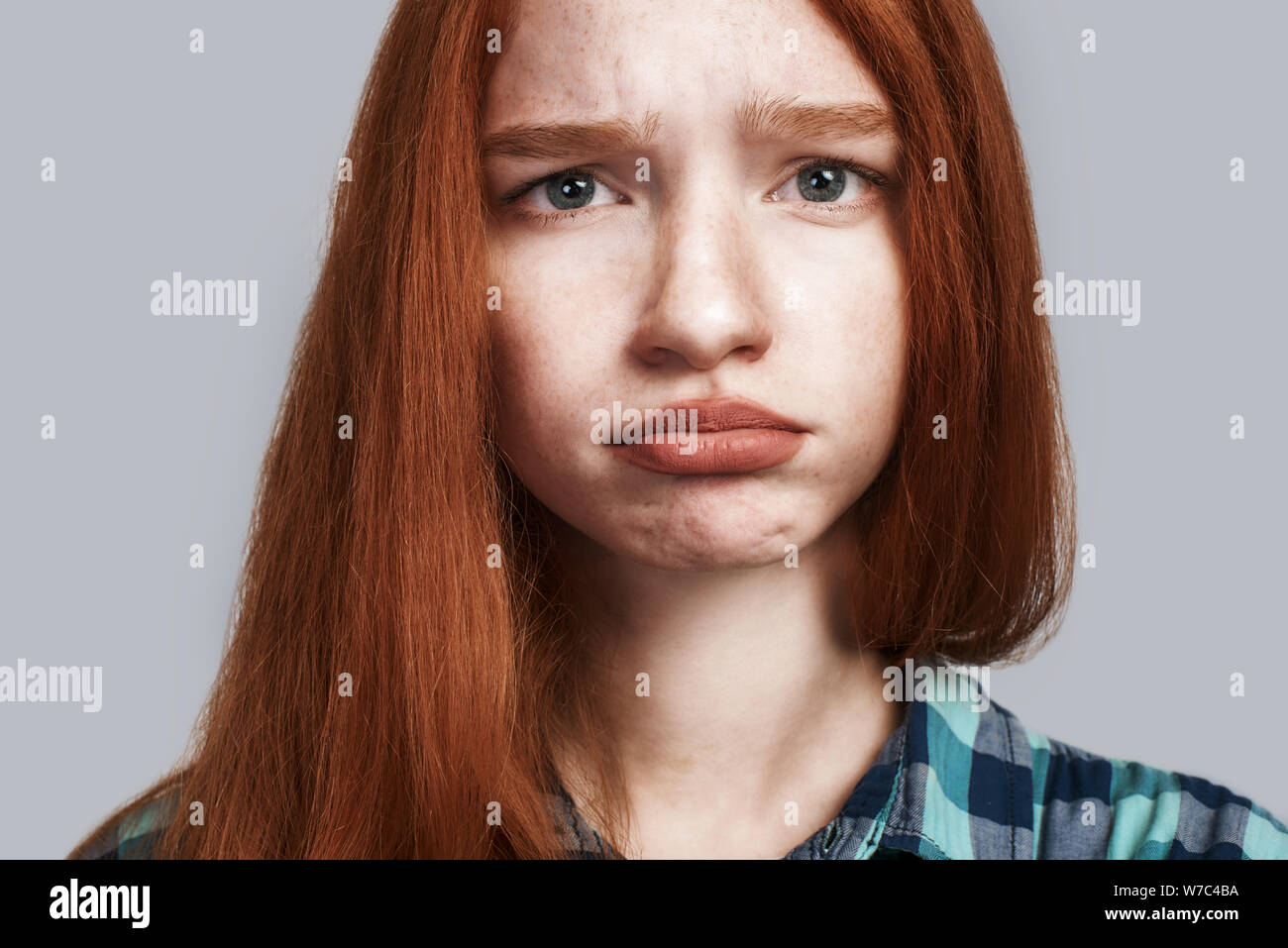 Studio shot of redhead girl in checkered shirt making sad face while ...