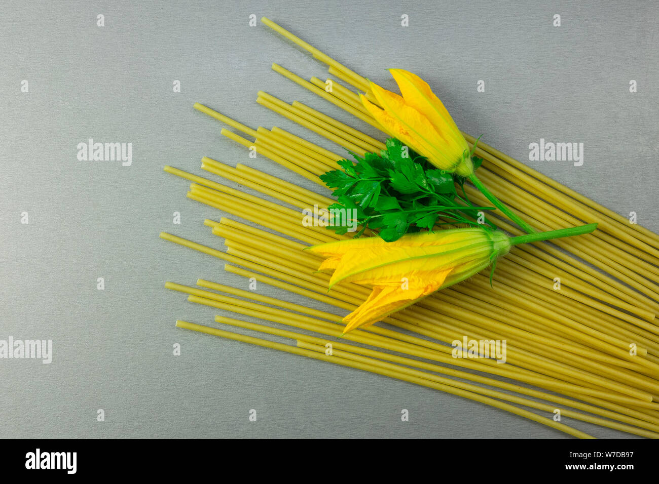 Spaghetti sticks, parsley leaves and yellow flowers on gray kitchen ...