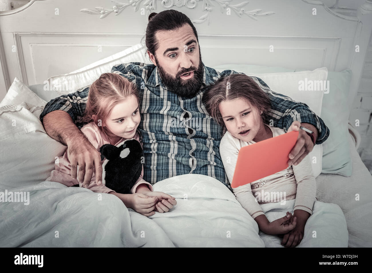 Interested in movie dad watching film on a tablet with daughters in bed ...