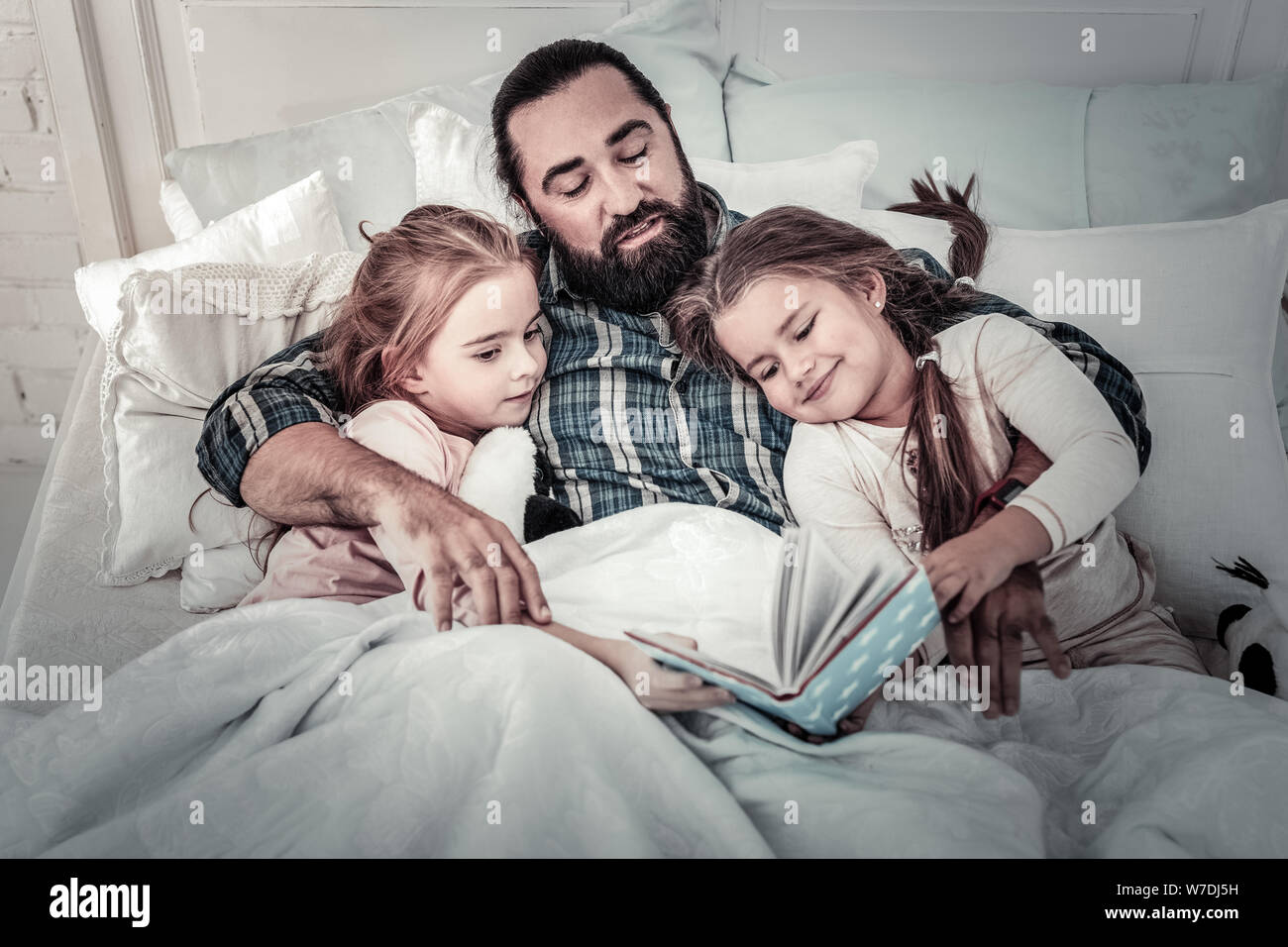 Dad and daughters cuddling in bed reading book Stock Photo - Alamy