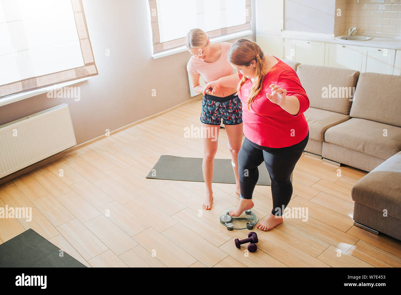 Young slim model help overweight woman to stand on weight scale in ...