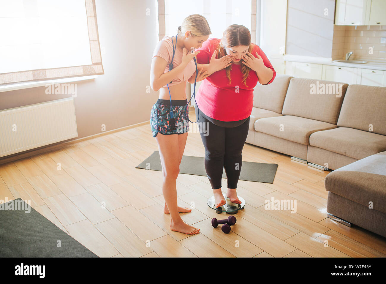 Young overweight and slim women in living room. Plus size model stand ...