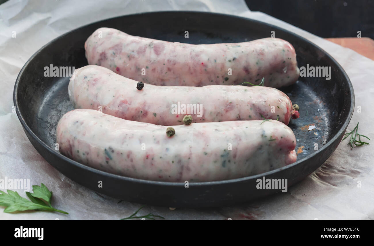 Fresh sausages with greens and spices for a barbecue on an iron griddle ...