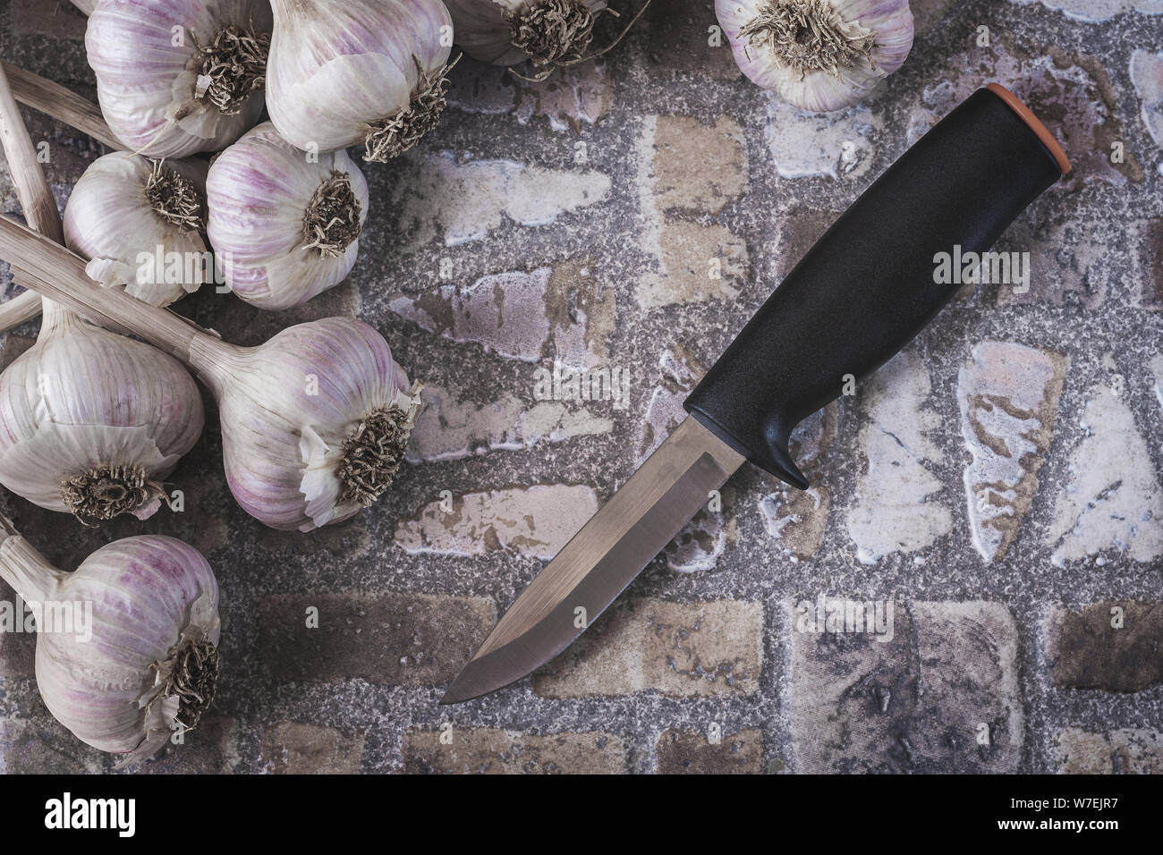 Frame made up of garlic bulbs with black knife on stone background ...
