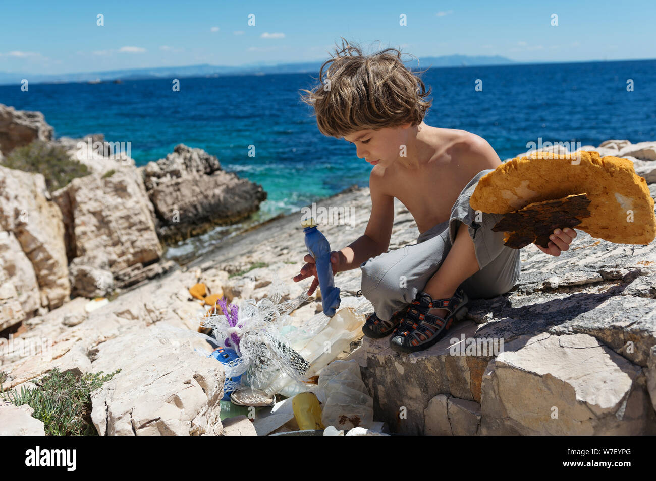 Little boy cleaning up beach full of rigid plastic bottles and other ...
