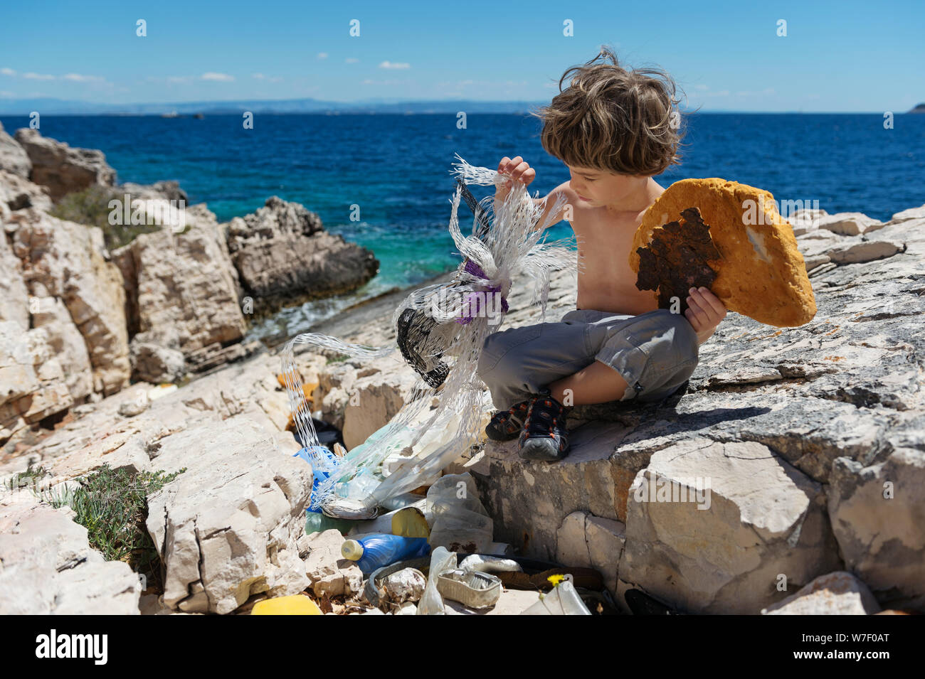 Little boy cleaning up beach full of rigid plastic bottles and other ...
