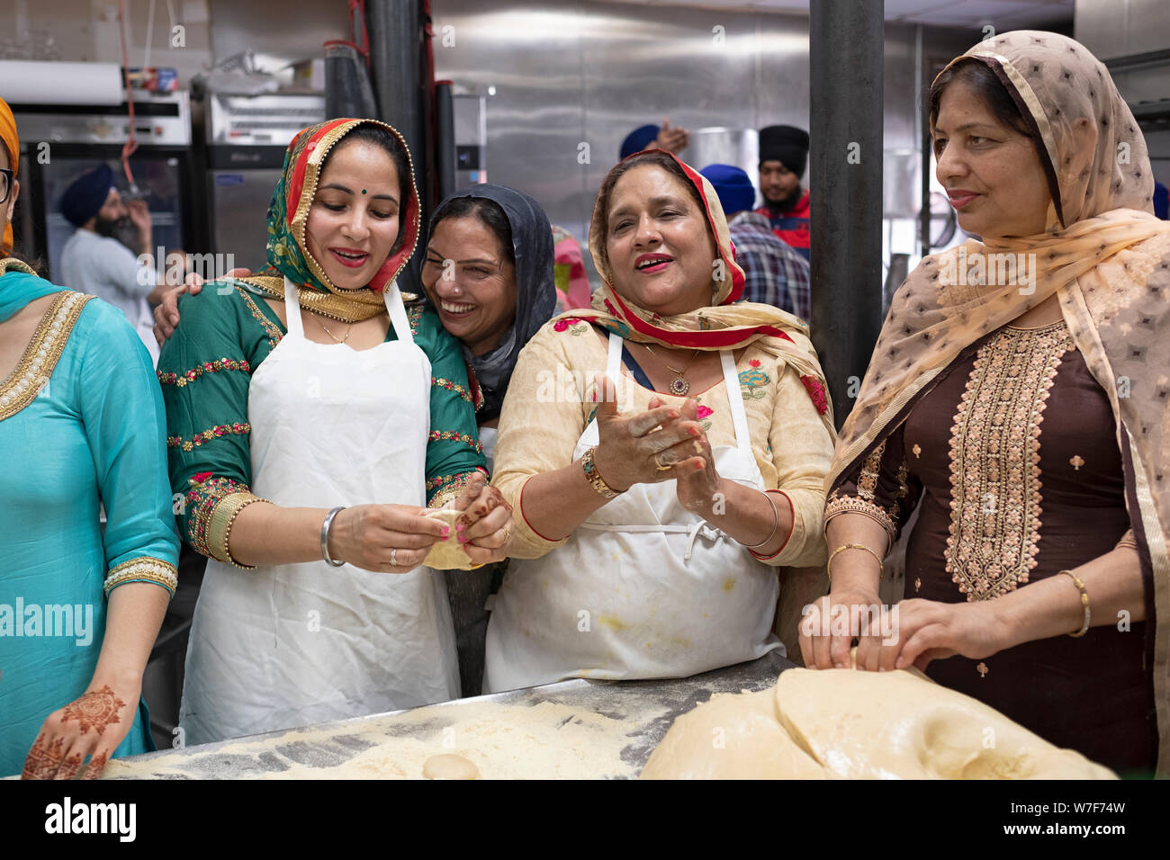 Volunteers of various ages share a laugh while making roti bread at a ...
