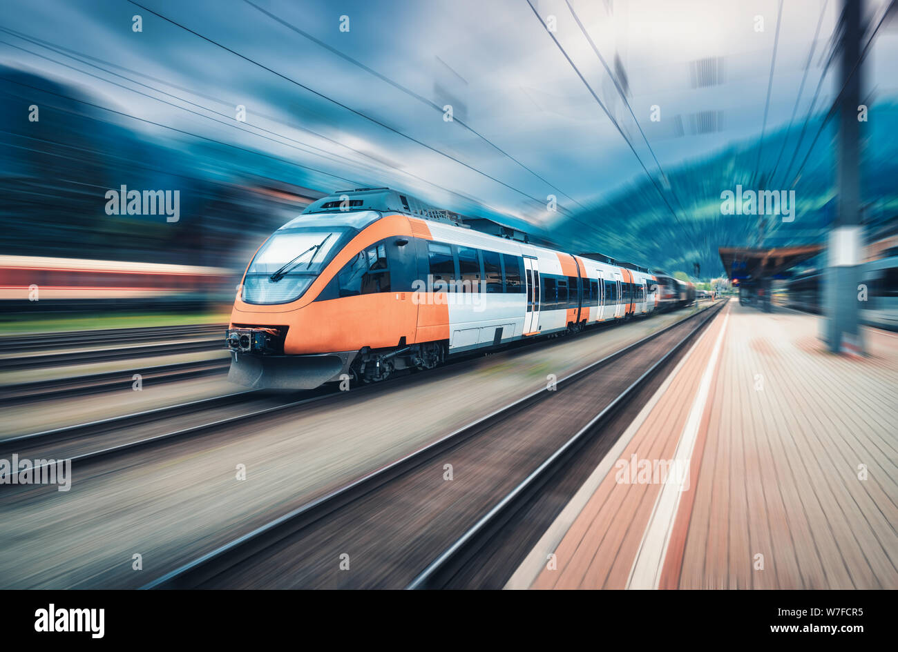 High speed orange train in motion on the railway station Stock Photo ...