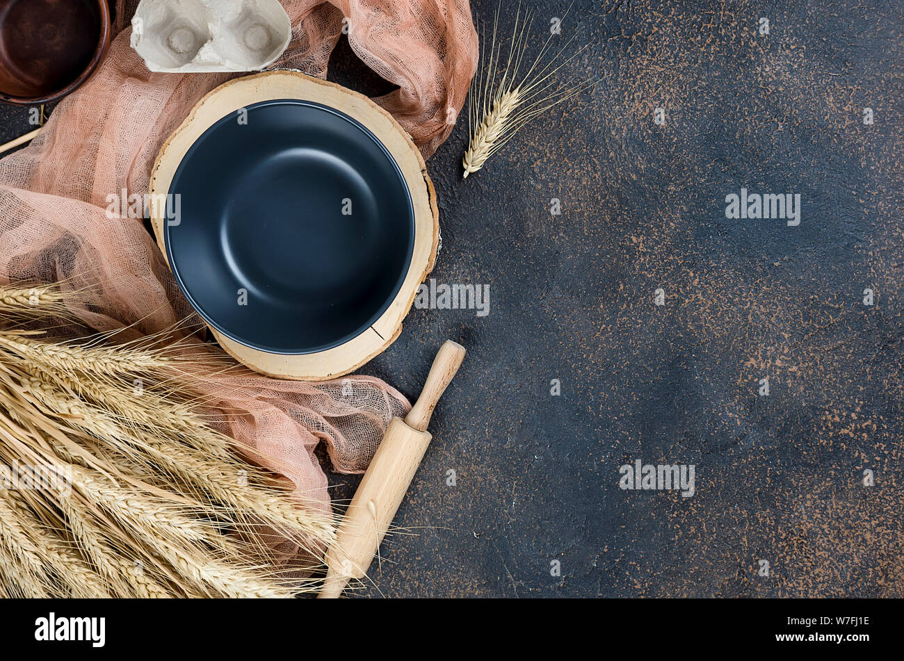 Empty bowl for raw dough and ingredients, eggs, flour, ears of wheat on ...
