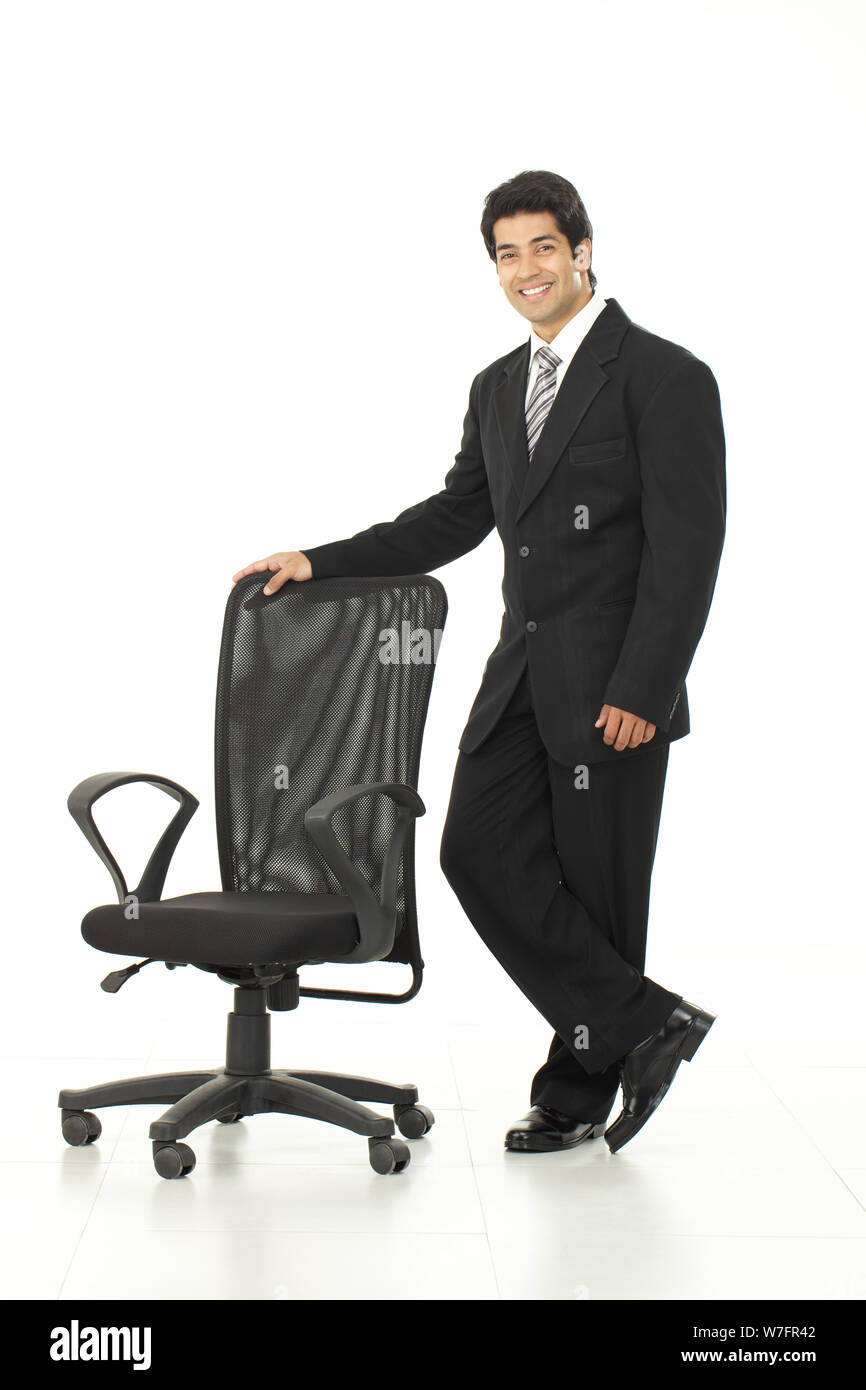 Businessman standing by a chair in an office Stock Photo - Alamy