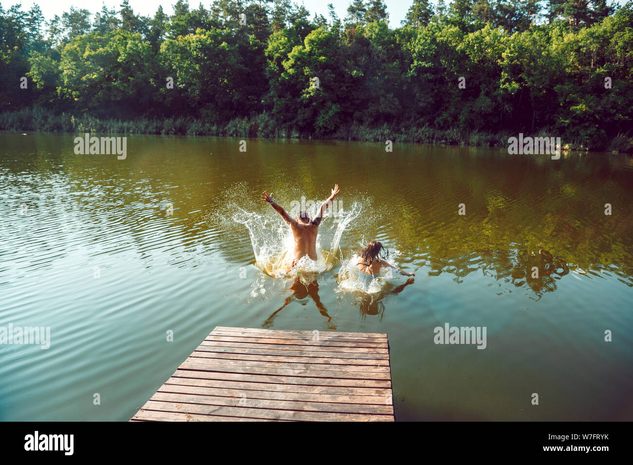 Happy friends having fun while laughting and jumping from the pier in ...