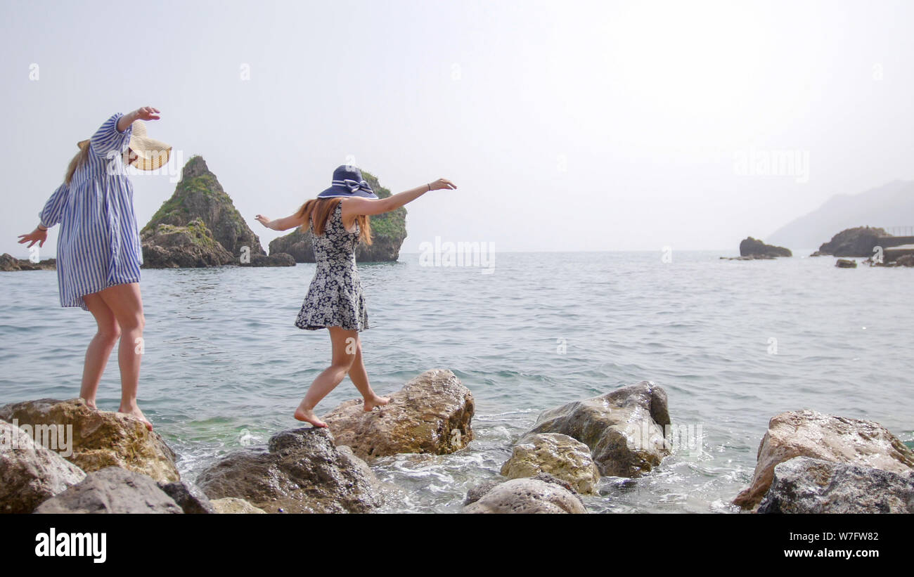 Two attractive women walking on the wet rocks by the sea Stock Photo ...
