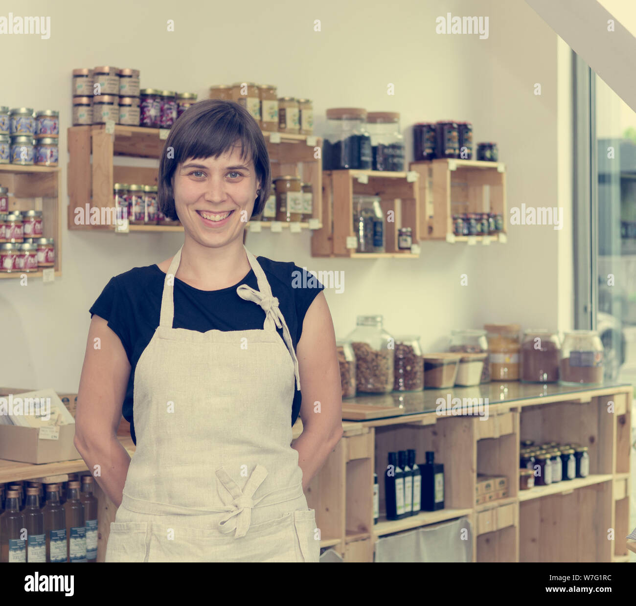 Cherfull young female shop owner posing in front of shelves full of ...
