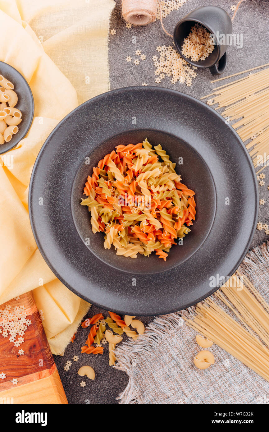 Different types of pasta on a black plate top view Stock Photo - Alamy