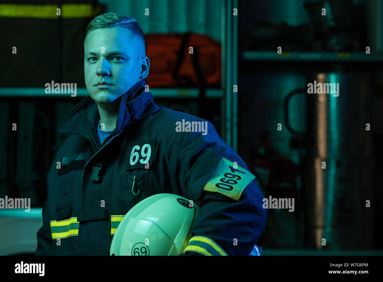 Photo of young fireman looking to camera with helmet in hand near fire ...