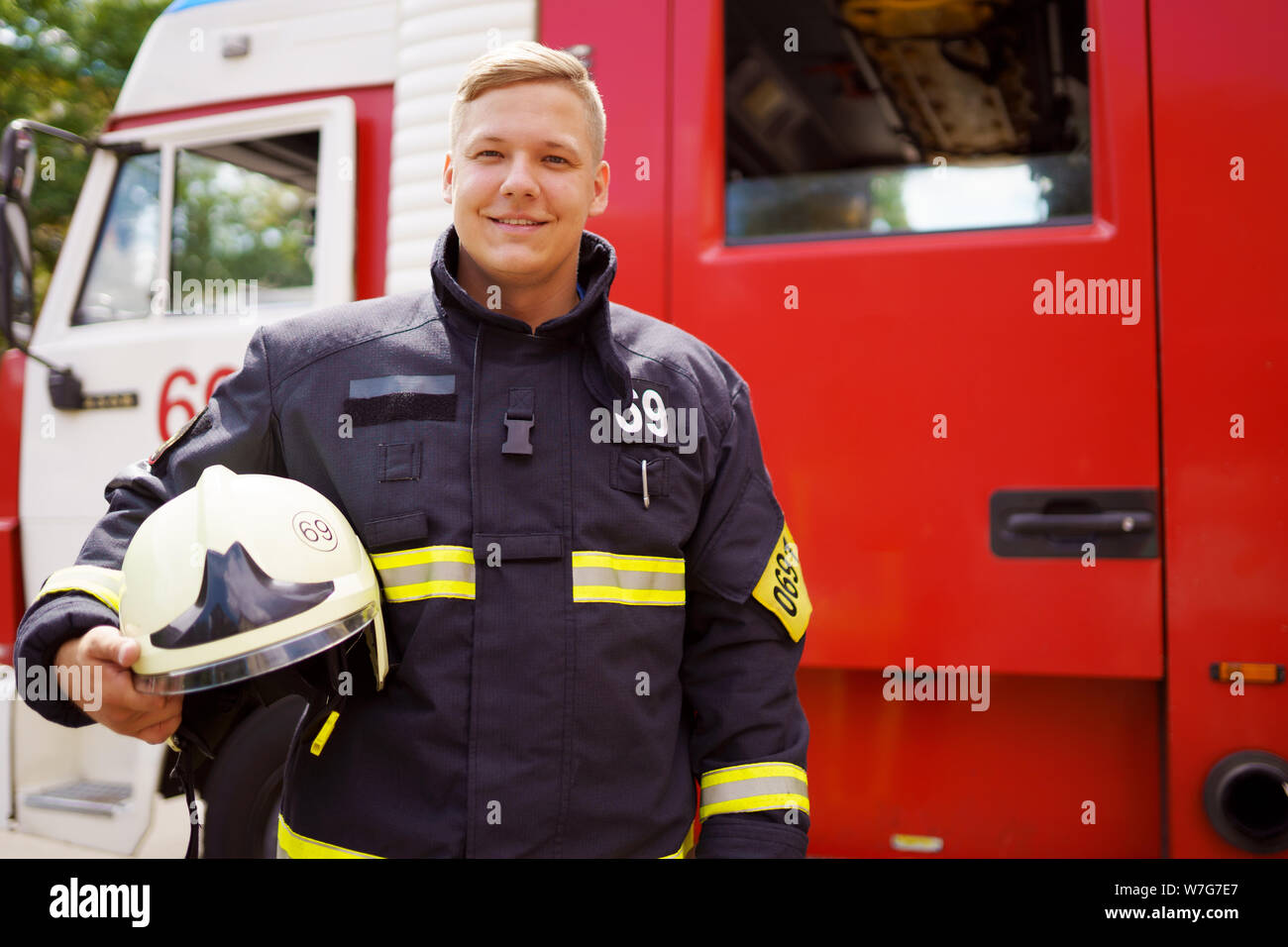 Photo of man firefighter with helmet in his hand standing near fire ...