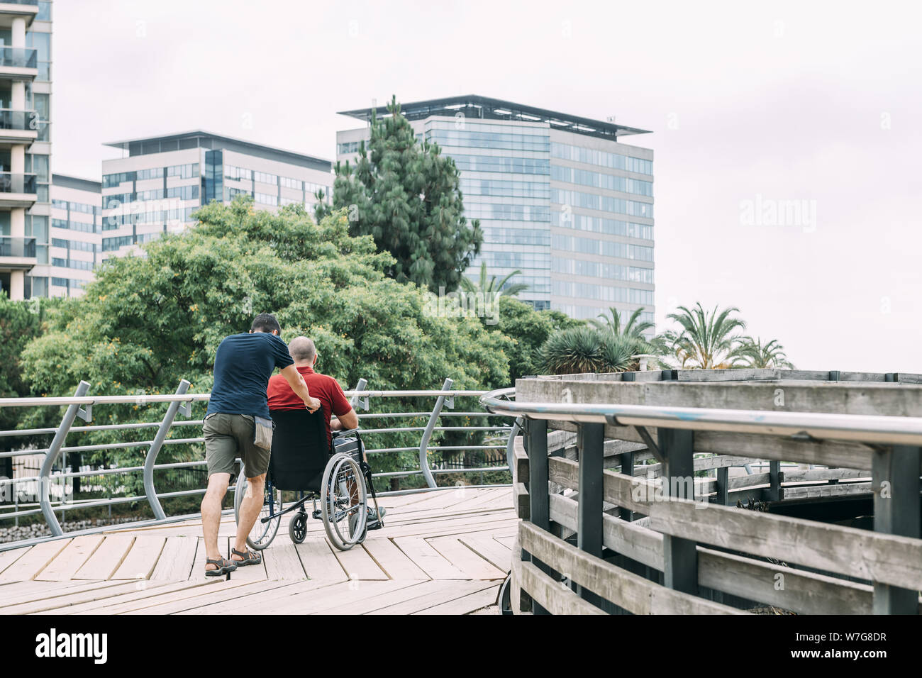 man pushes his disabled friend's wheelchair into the city, concept of ...