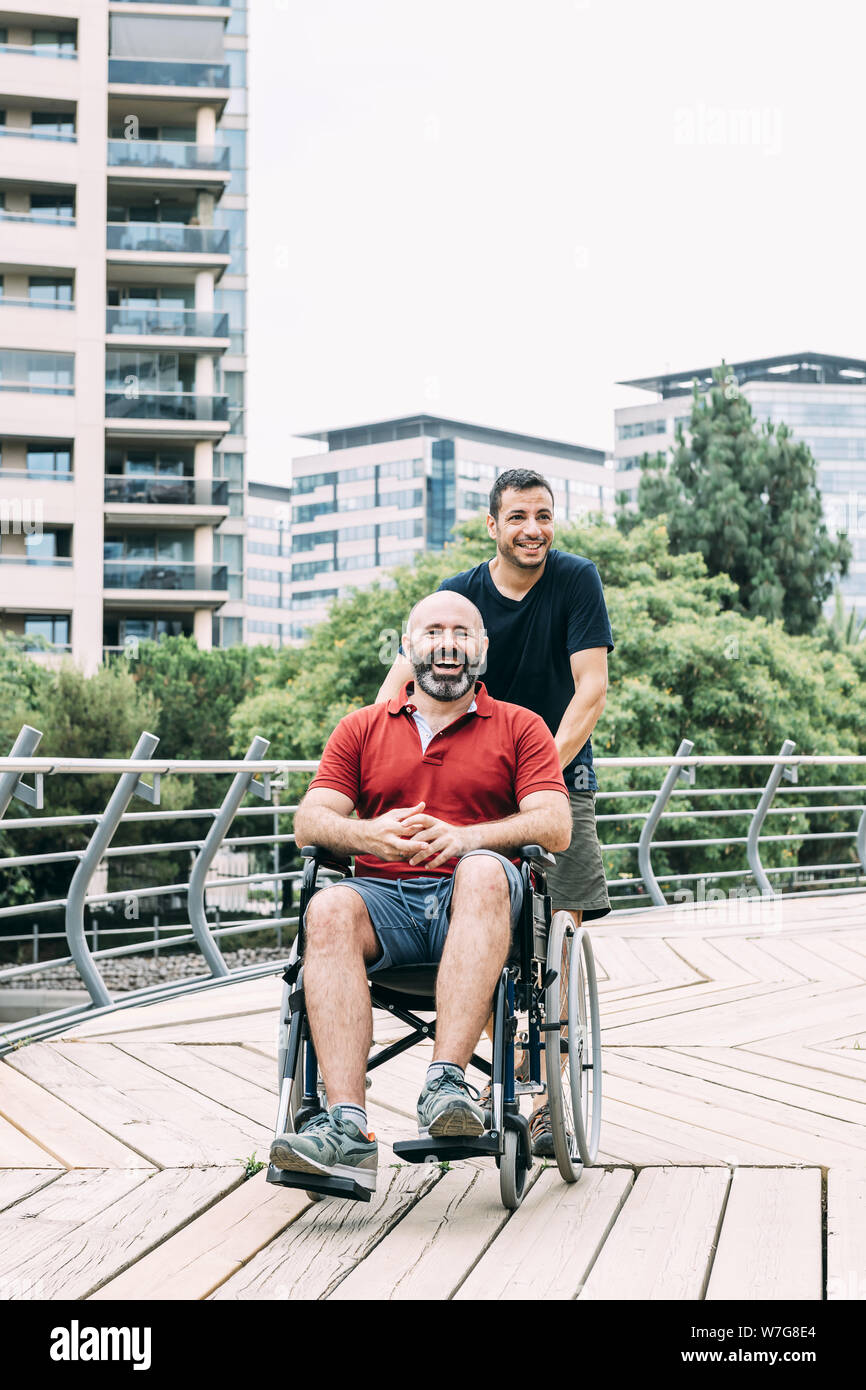 disabled man in wheelchair laughing during a walk with a friend at park ...