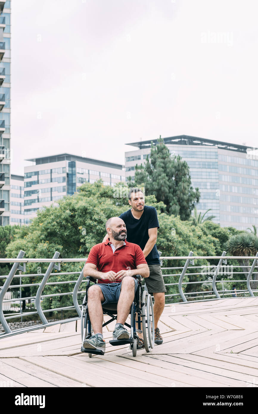 disabled man in wheelchair walks with his friend through the city ...