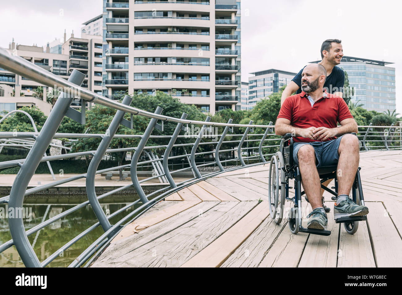 disabled man in wheelchair converses with his friend during a walk ...