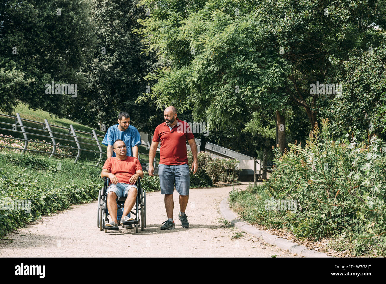 disabled man in a wheelchair walking with his caretaker and a friend at ...