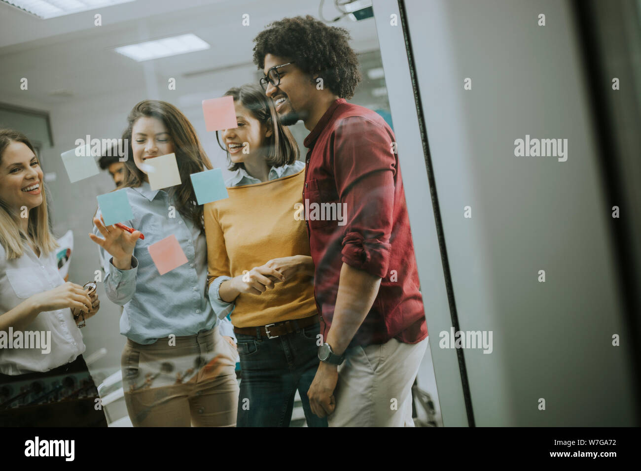 Group of young business people discussing in front of glass wall using ...