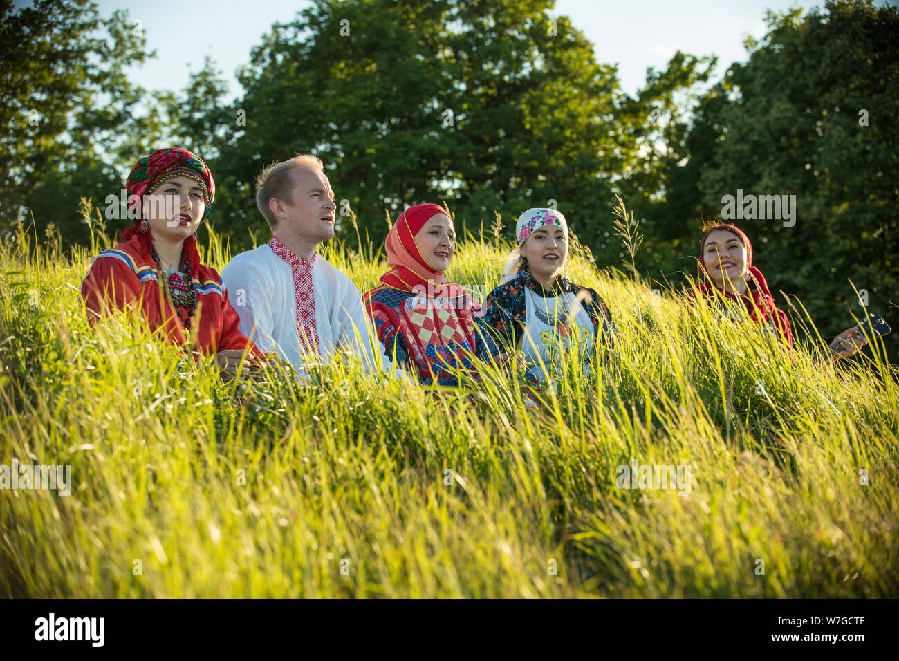 Smiling people in traditional russian clothes sitting on the field in ...
