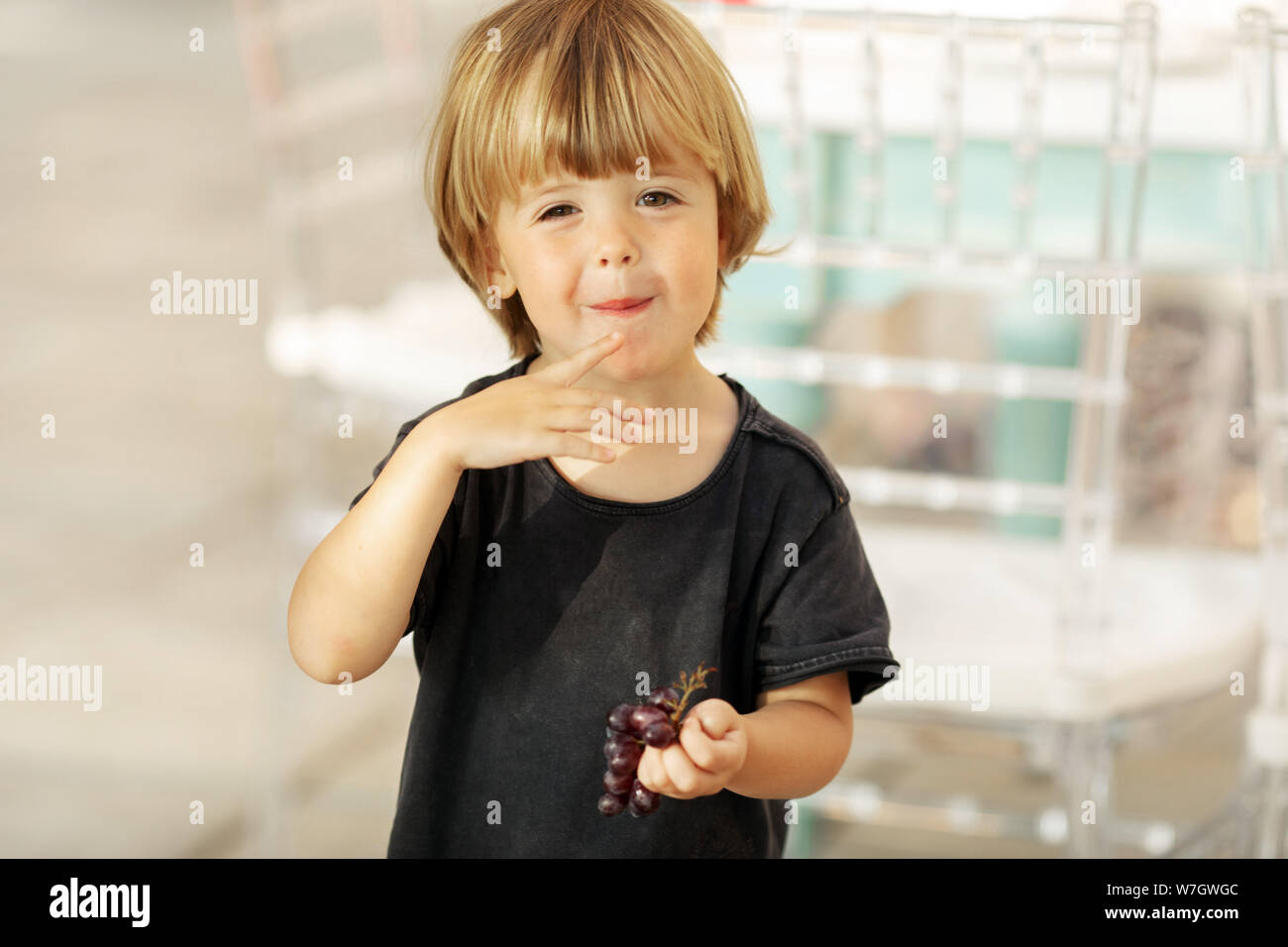 Happy kid eating grapes in light room Stock Photo - Alamy