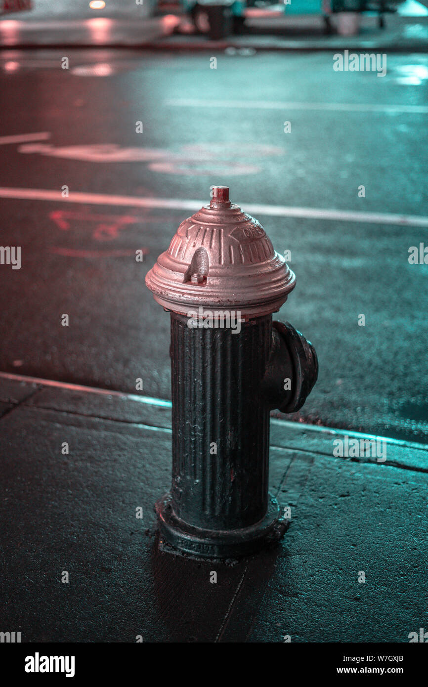 A water hydrant painted black and purple in the street at night - Close ...