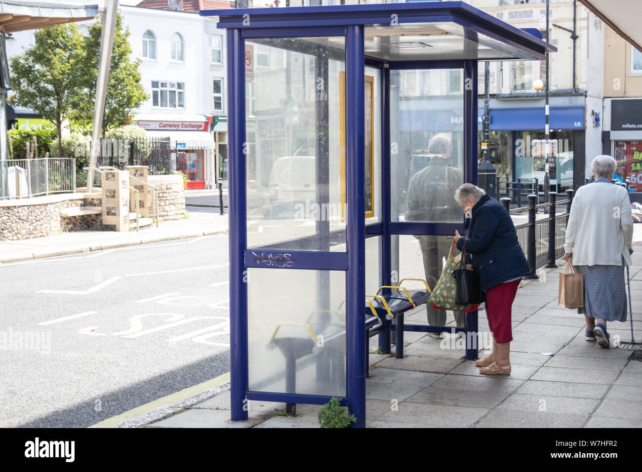 An elderly lady waiting at a bus stop for her bus to arrive Stock Photo ...