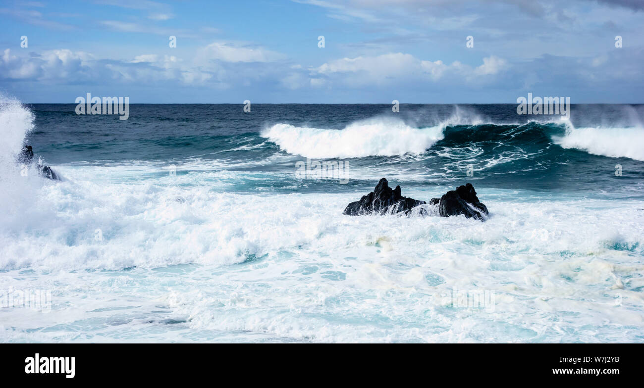 Powerful ocean waves crashing and churning on jagged basalt rocks, in ...