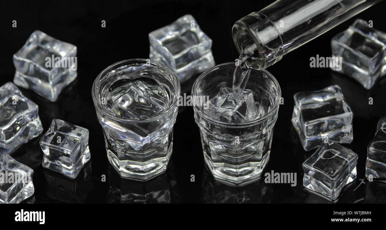 Pouring up shots of vodka from a bottle into drinking glass against ...