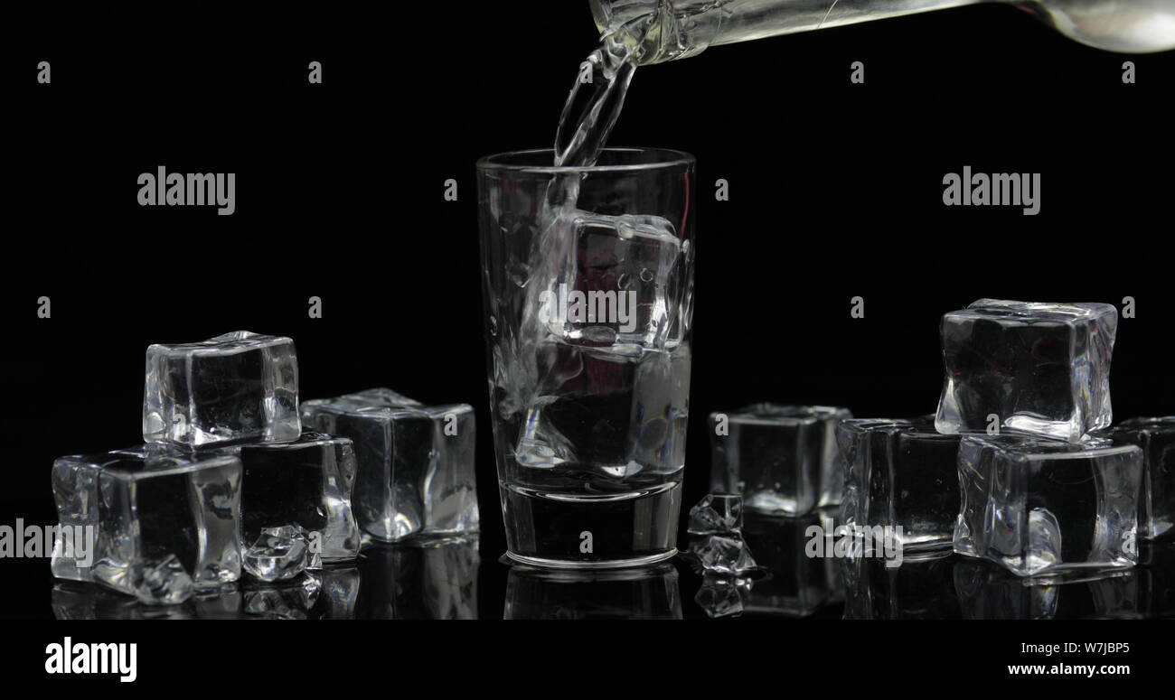 Pouring up shot of vodka from a bottle into drinking glass against ...