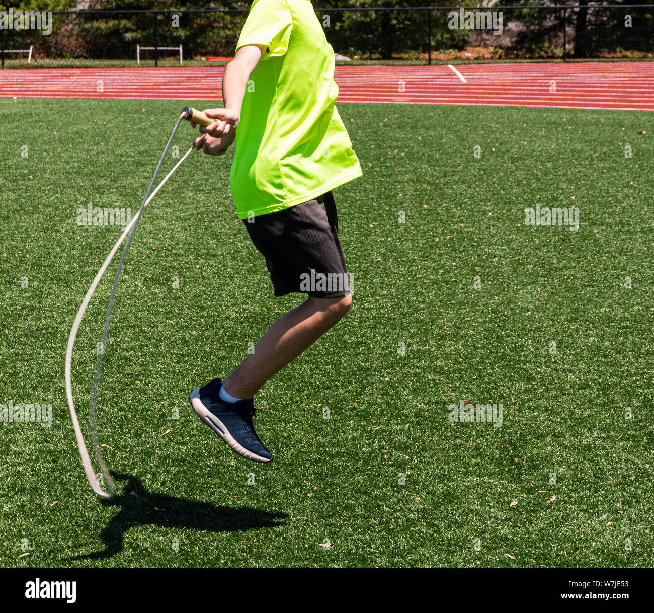Side Veiw of a high school boy is jumping rope on a green turf field ...