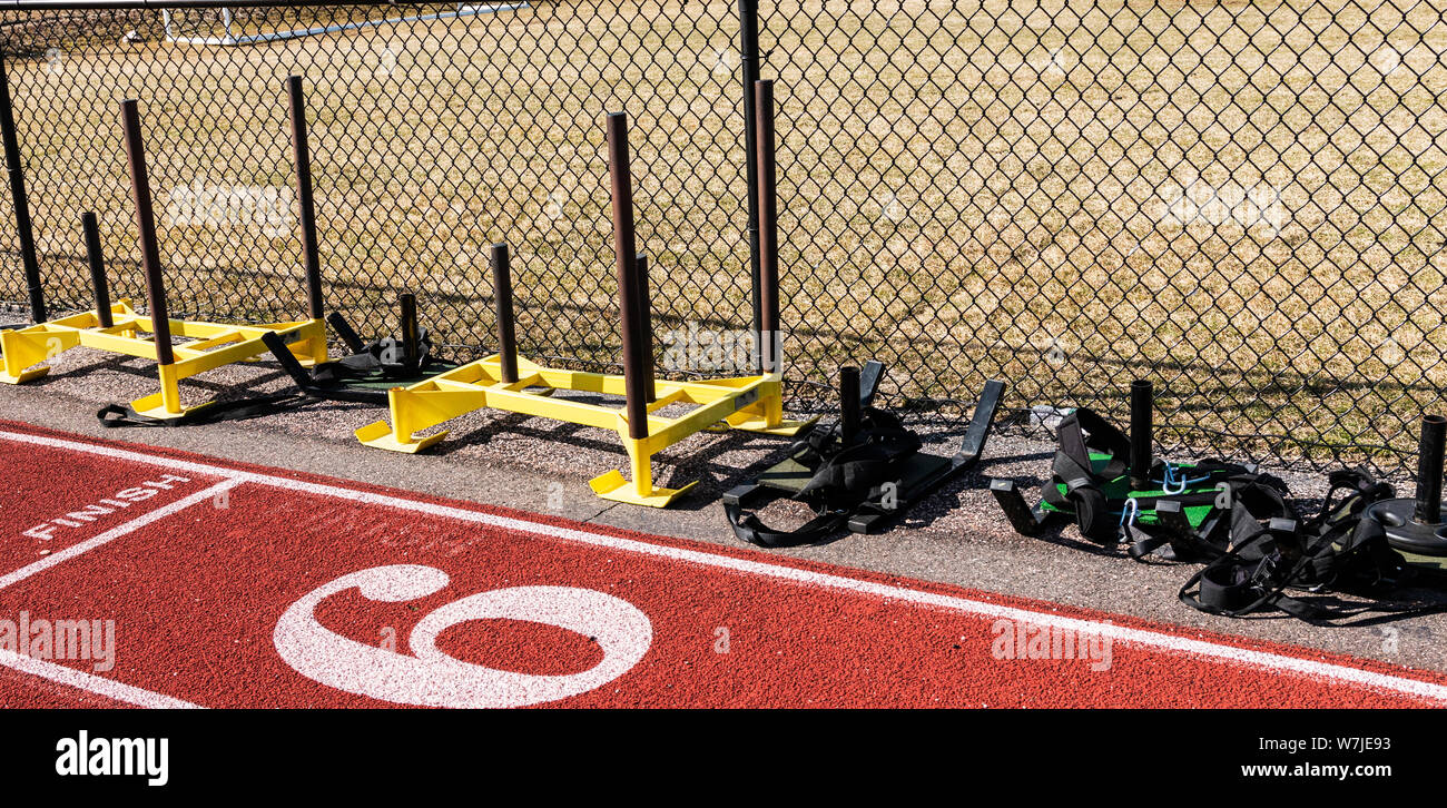 Push and pull weight sleds against a fence on the side of a red next to ...