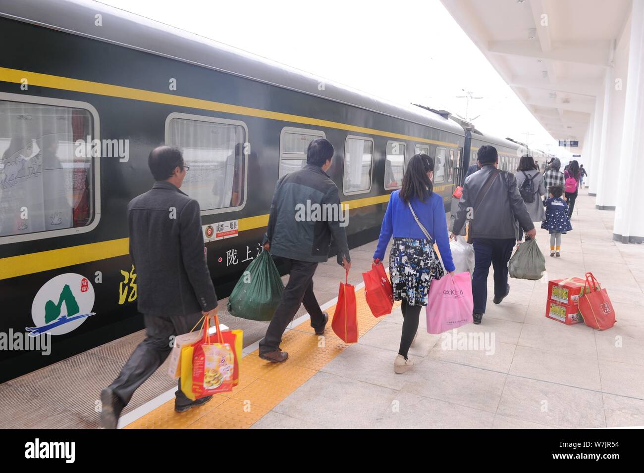 Chinese passengers walk past a train on the Lanzhou-Chongqing railway ...