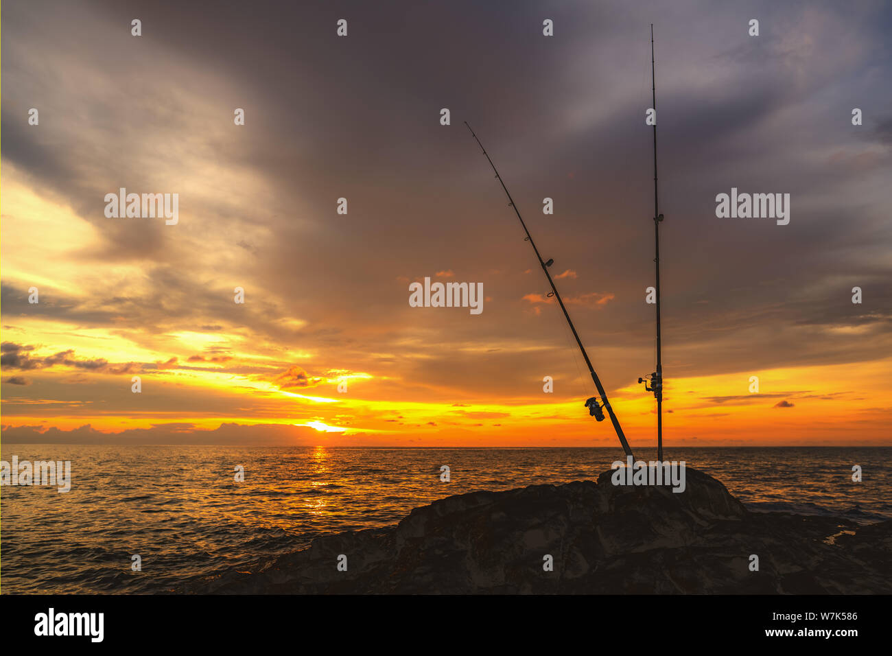 fishing rods on the background of a beautiful orange sunset on the sea ...