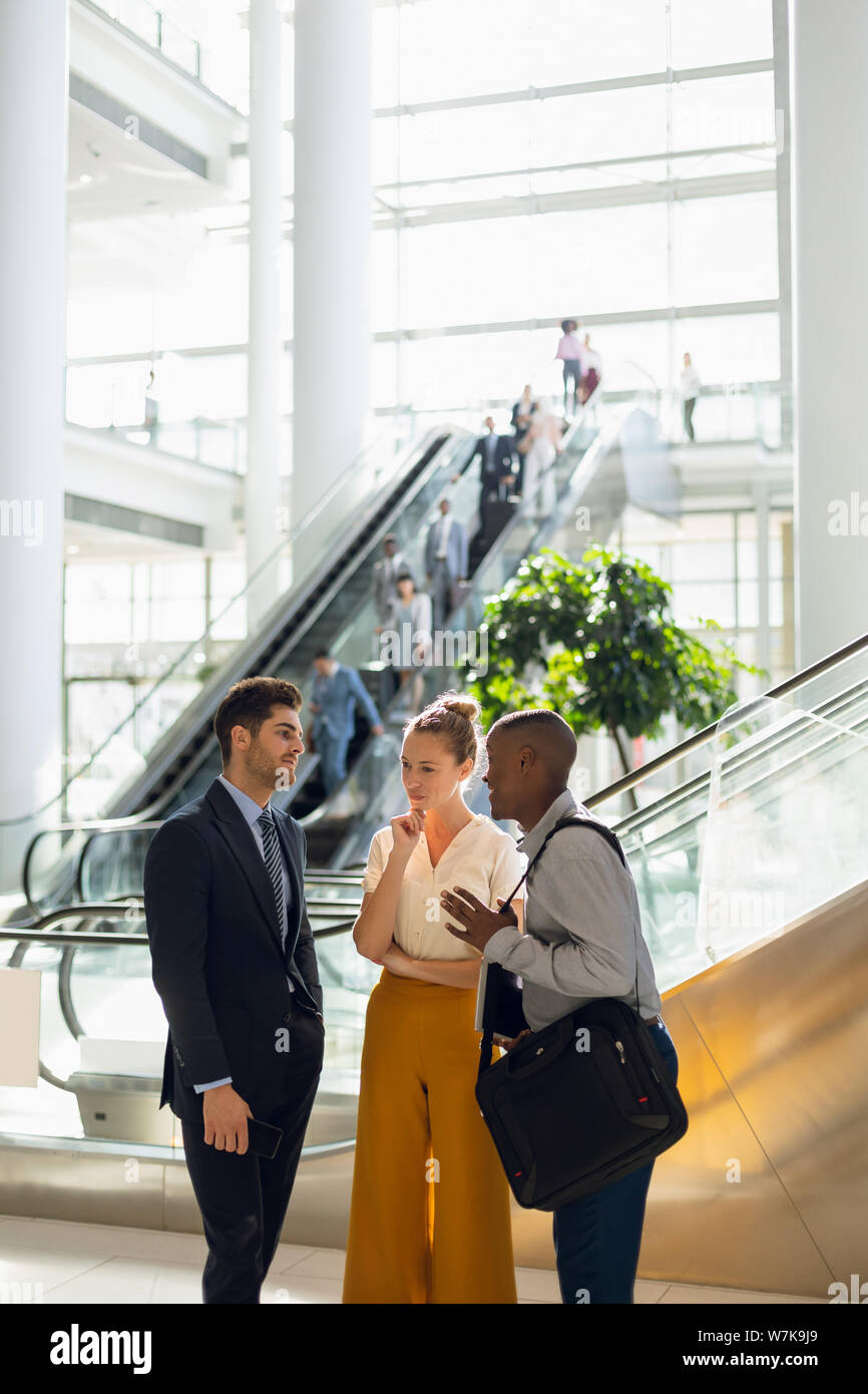Three diverse young business people talking in the atrium of a modern ...