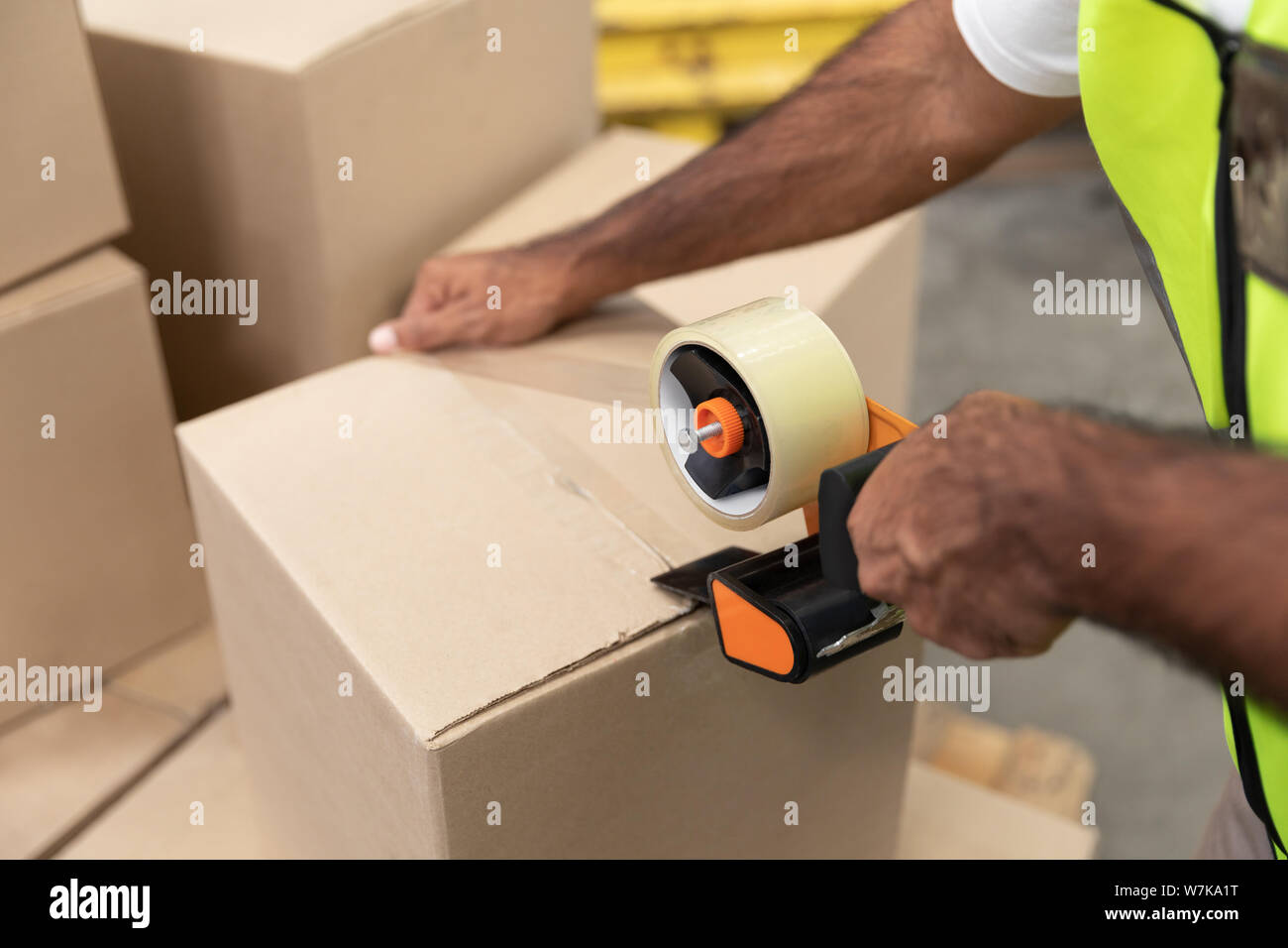 Male worker packing cardboard box with tape gun dispenser in warehouse ...