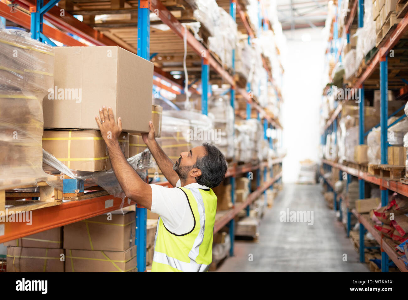 Male worker putting cardboard box on a rack in warehouse Stock Photo ...