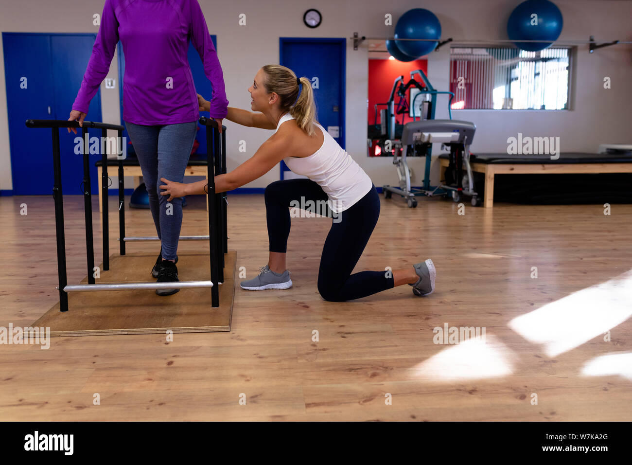 Female physiotherapist helping disabled senior woman walk with parallel ...