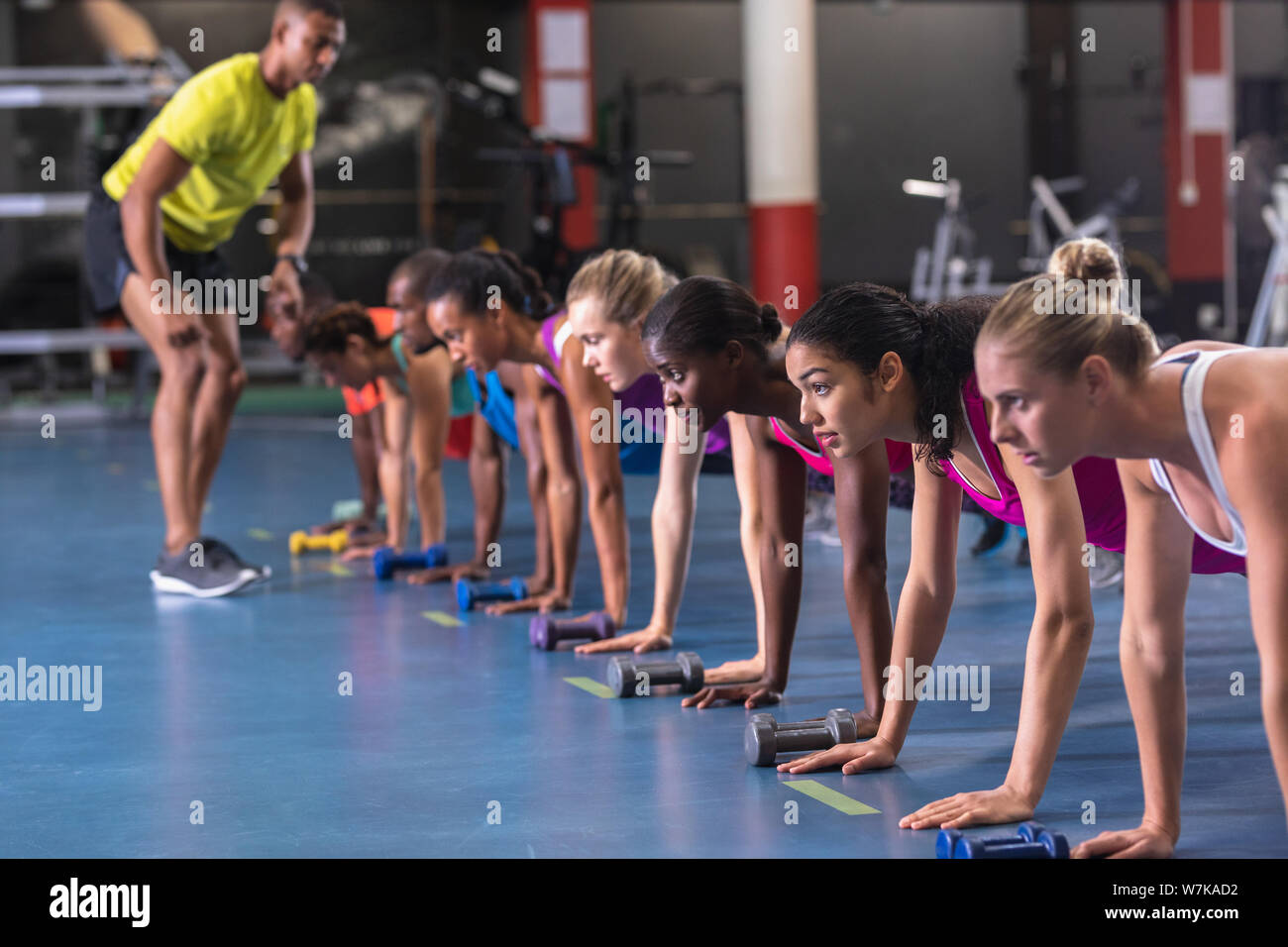 Male trainer training people to perform exercise in fitness center ...
