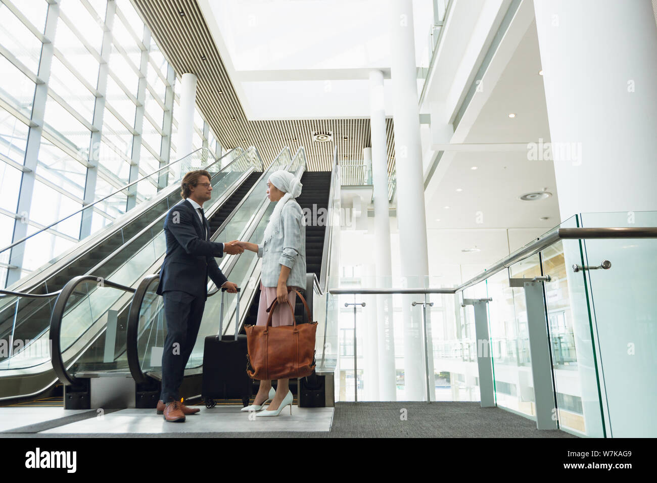 Business people shaking hands with each other near escalator in a ...