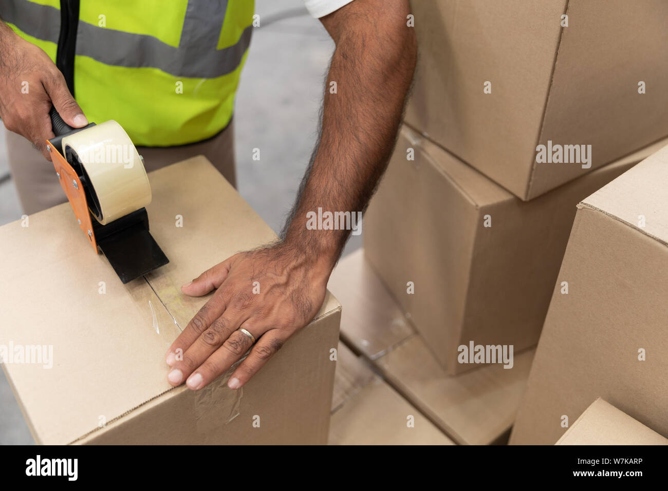 Male worker packing cardboard box with tape gun dispenser in warehouse ...