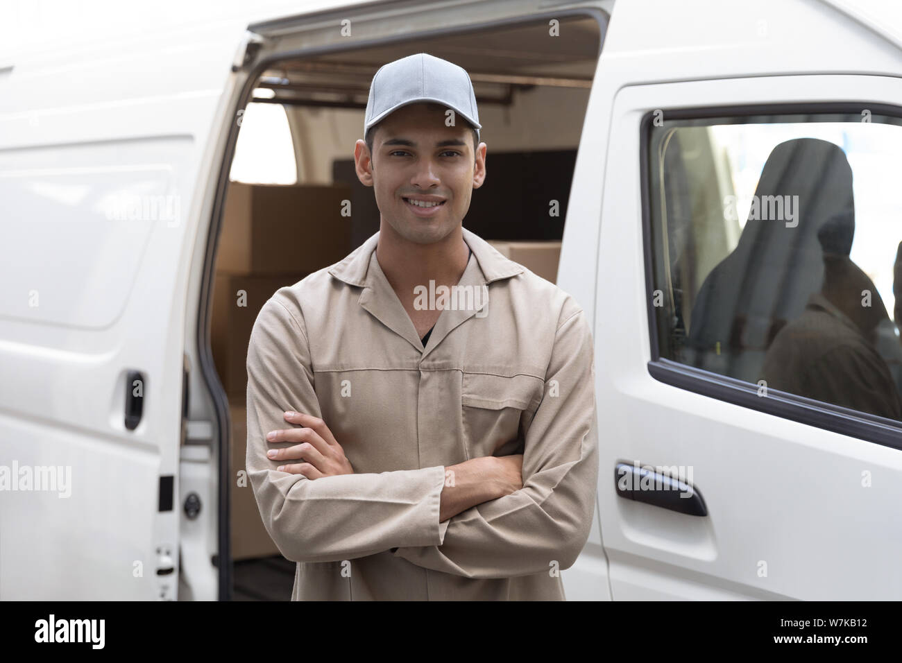 Delivery man standing with arms crossed near van outside the warehouse ...