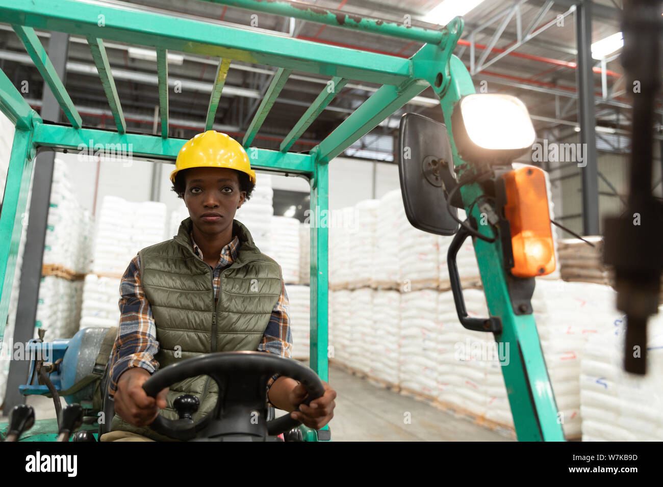 Female worker looking at camera while driving forklift in warehouse ...