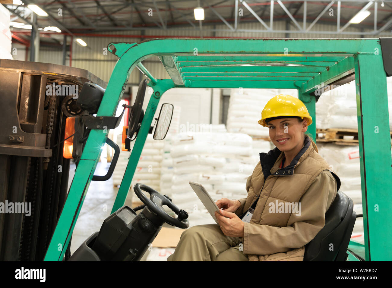 Female worker using digital tablet while sitting in forklift in ...