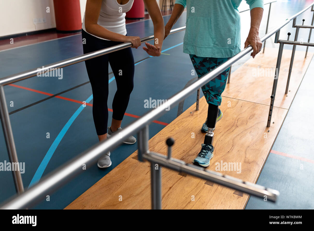 Female physiotherapist helping disabled senior woman walk with parallel ...