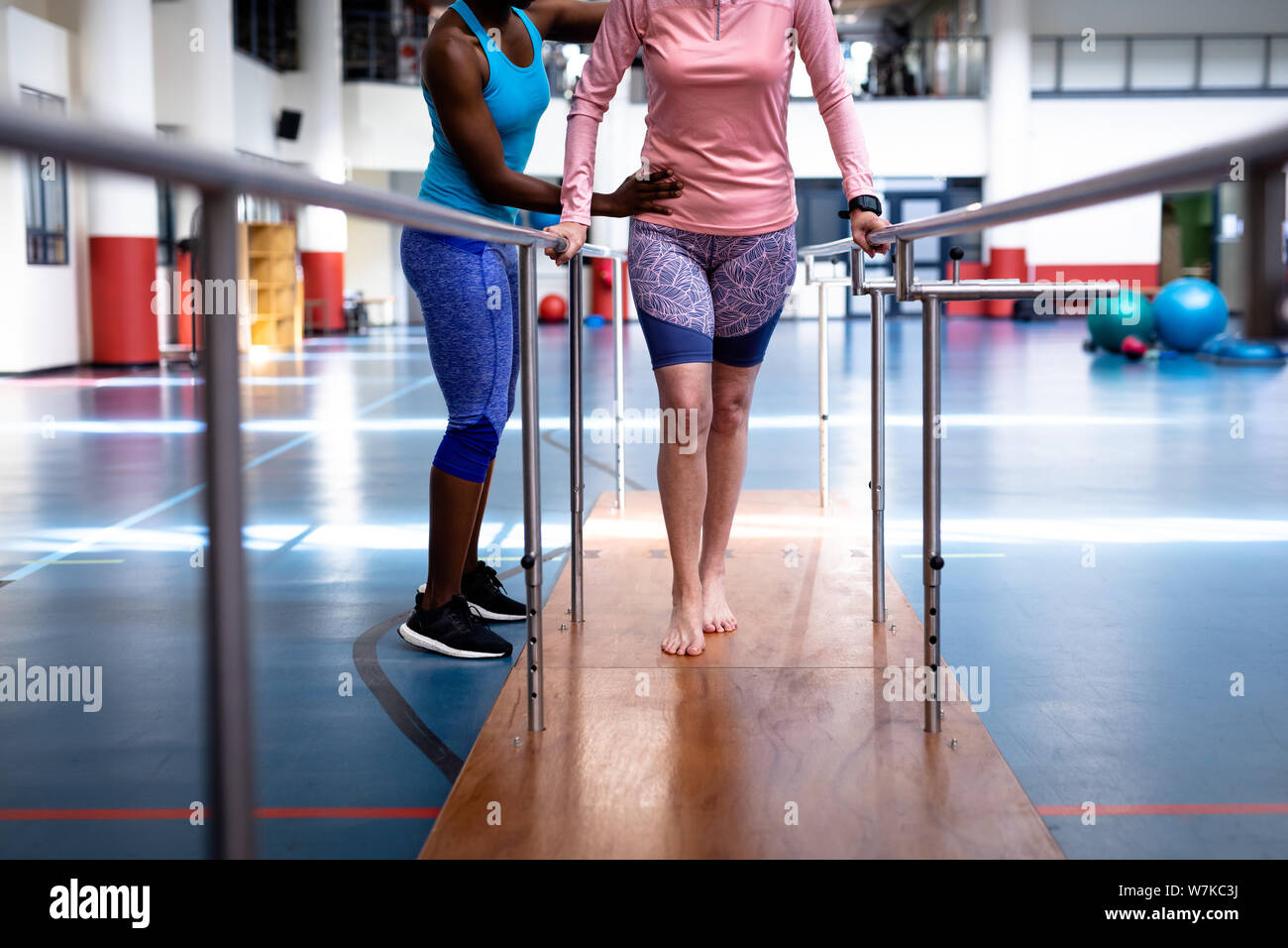 Female physiotherapist helping disabled senior woman walk with parallel ...
