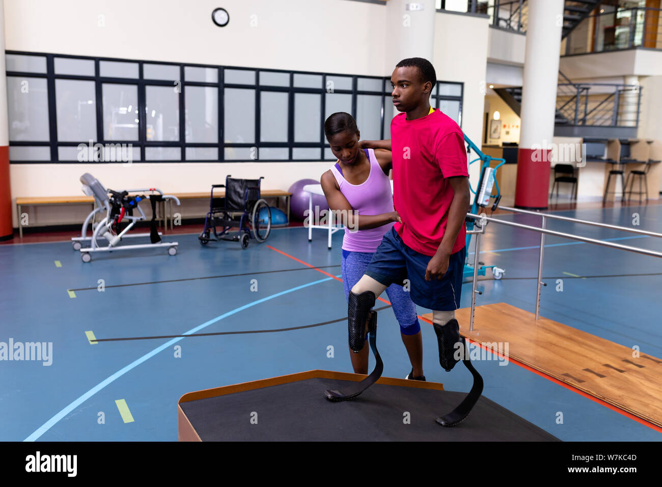 Physiotherapist helping disabled man walk with prosthetic leg on ramp ...